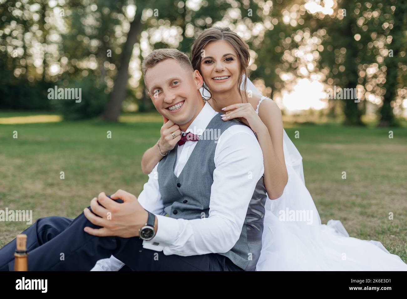 Portrait of beautiful wedding couple sitting on green grass in park in ...