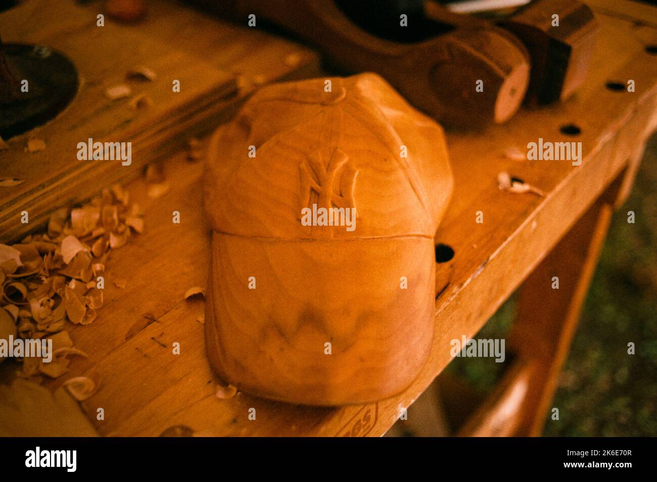 A hand carved wood Yankeys baseball hat rests on woodworking bench with ...