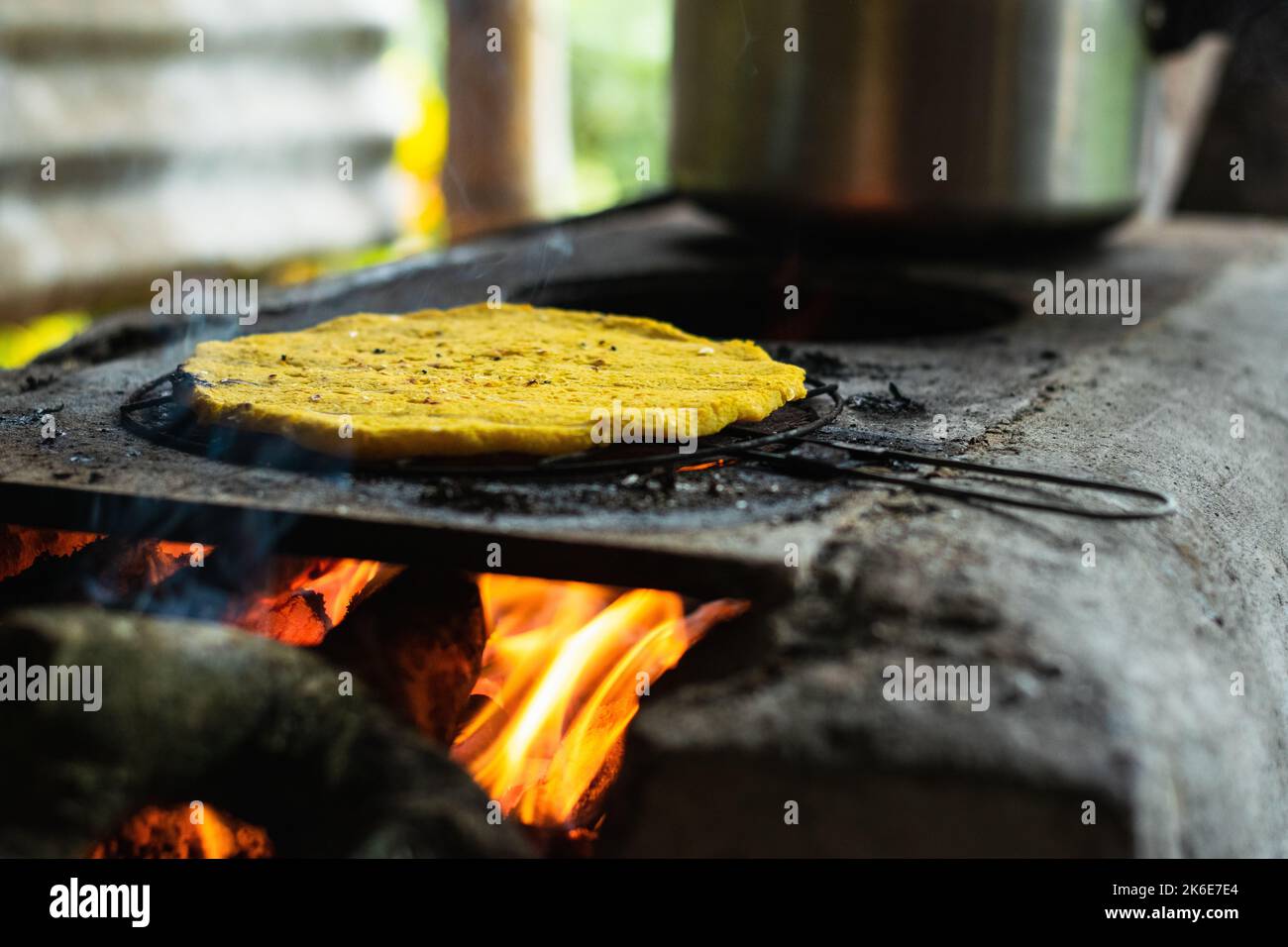 detailed view of a yellow arepa being grilled on a handmade brick stove ...