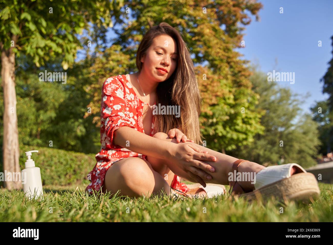 woman putting sunscreen on body sitting on grass Stock Photo - Alamy