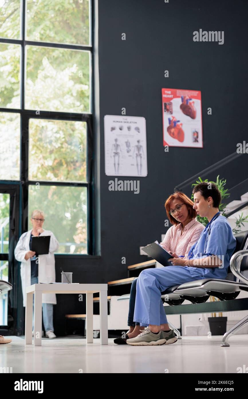 Medical asisstant consulting senior patient in hospital waiting area ...
