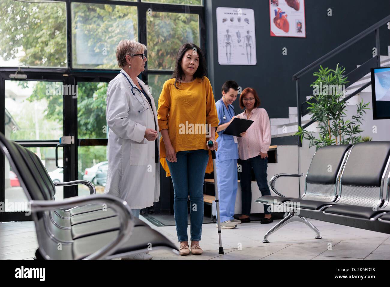 Senior physician helping injured patient to walk with stick, suffering ...