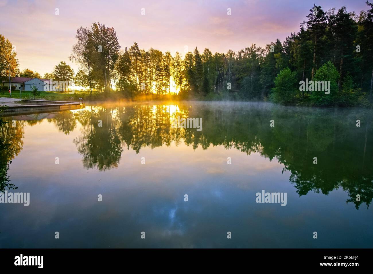 A beautiful view of a reflective bathing pond in a forest during sunset ...