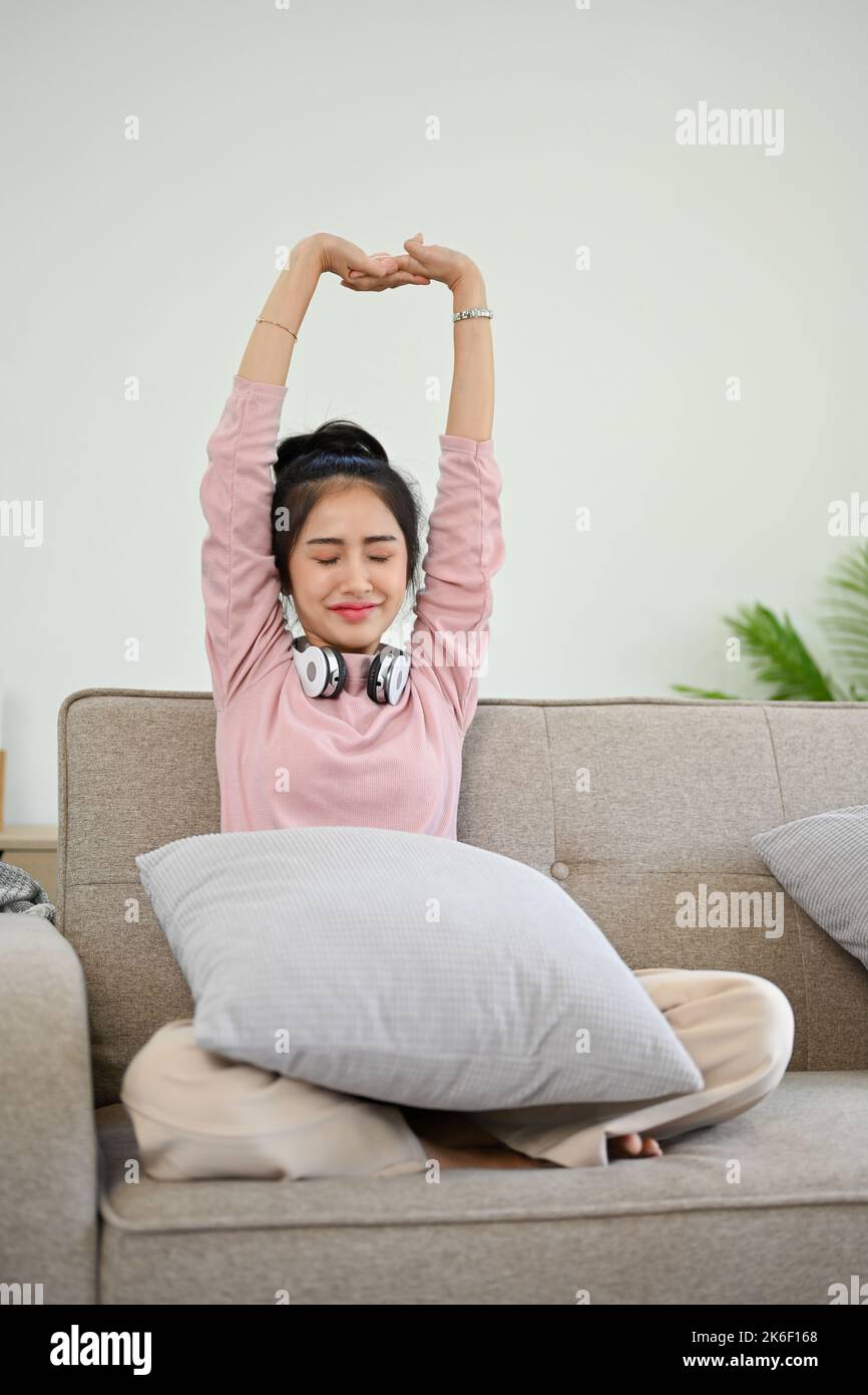 Relaxed young Asian female in casual clothes stretching her arms ...