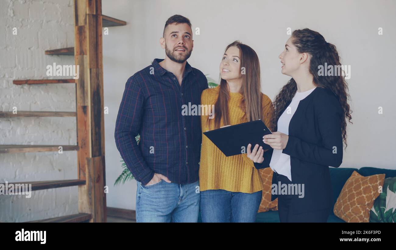 Cheerful house agent is talking to buyers adorable young couple ...
