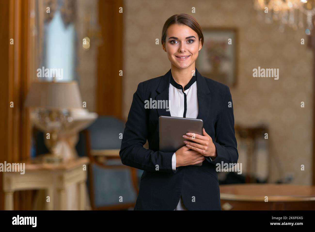 Smiling businesswoman in suit standing in hotel room using digital ...