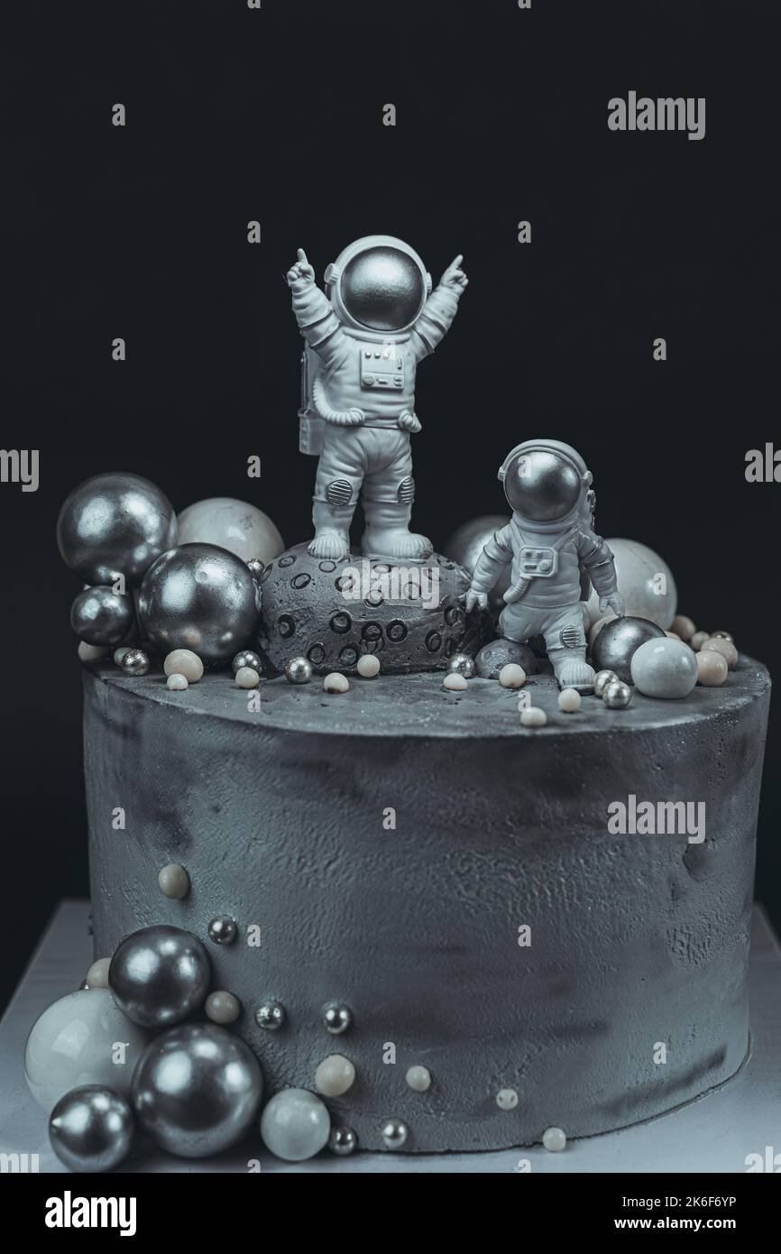 A gray cake imitating the surface of the moon and two astronaut figures ...