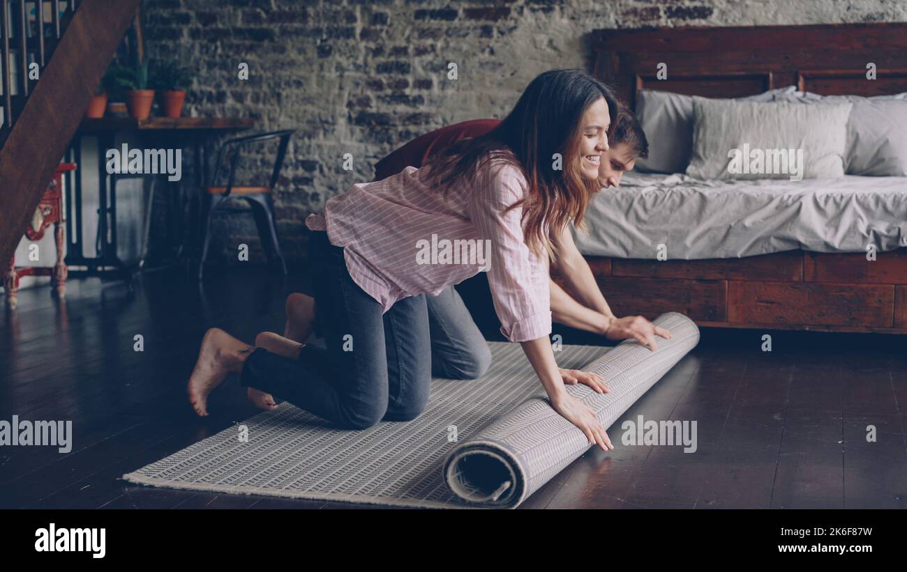 Happy husband and wife are unrolling carpet in their new house enjoying ...