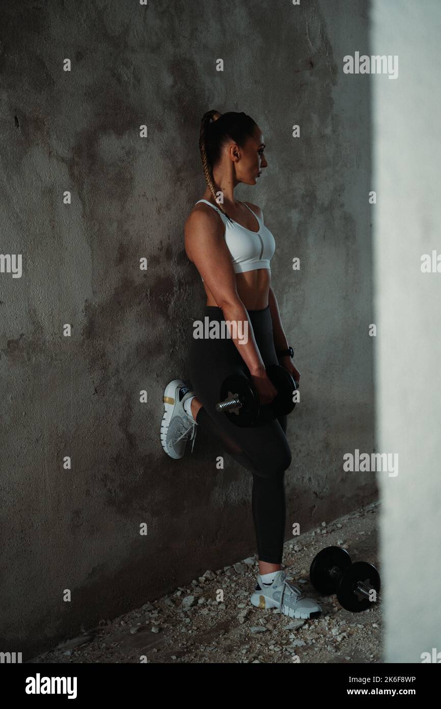 Sporty young girl leaning her left leg on the wall, looking left ...