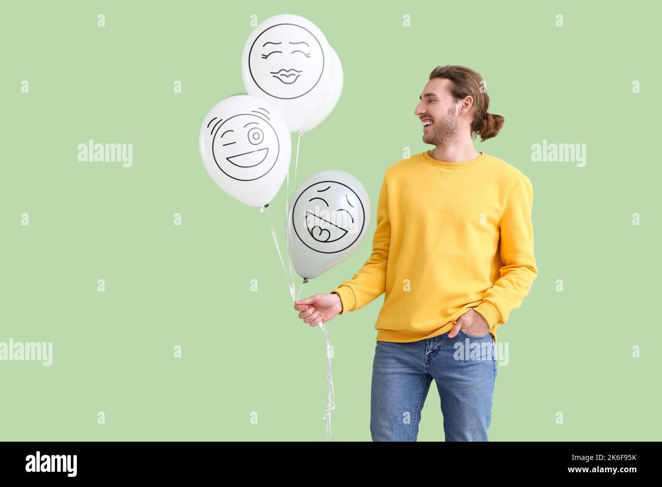 Happy young man holding balloons with drawn emoticons on green ...
