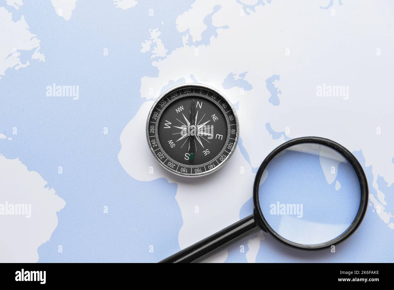 Magnifier and vintage compass on world map Stock Photo - Alamy