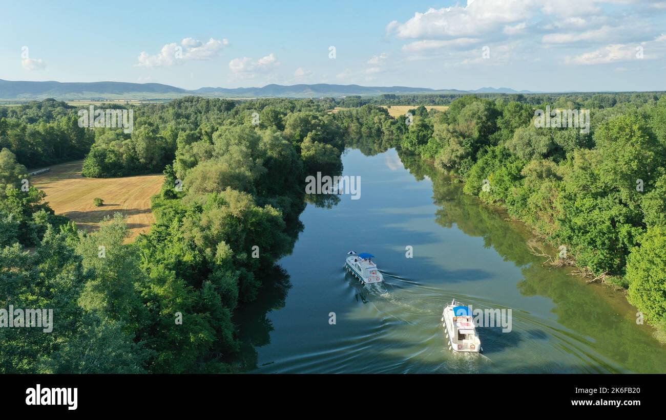 A narrow river surrounded by green trees with two boats on the water ...