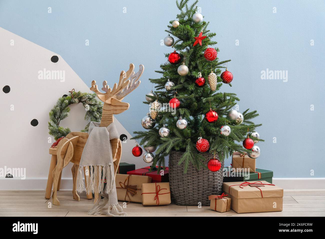 Wooden reindeer with scarf, Christmas tree and presents near color wall ...