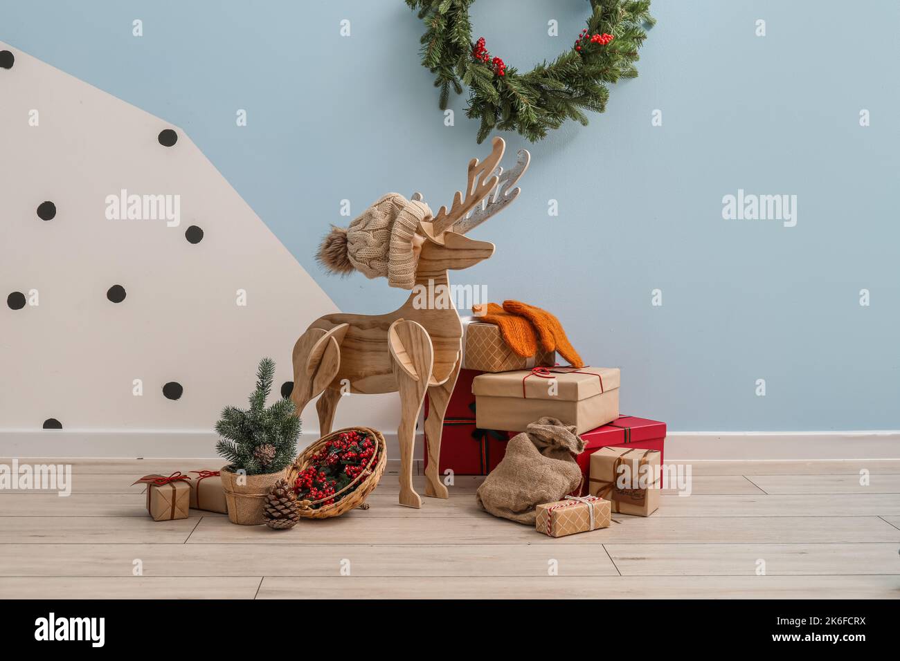 Wooden reindeer with hat, Christmas tree and presents near color wall ...