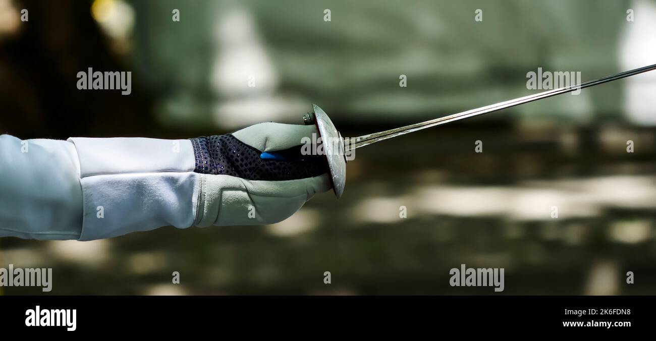 Epee of fencer with protected hand and arm against blurred background ...