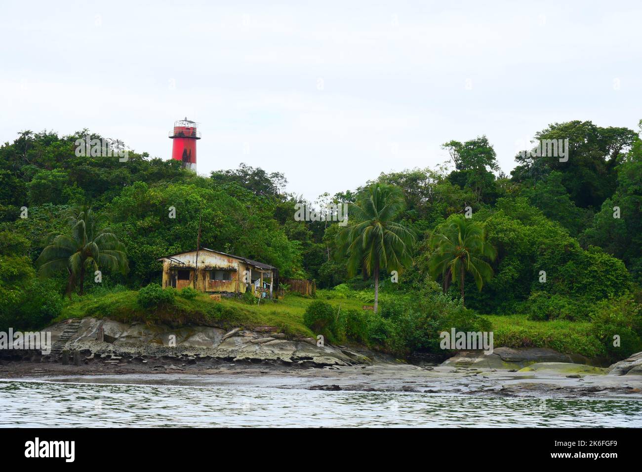 An old lighthouse near the shore surrounded by tropical plants ...