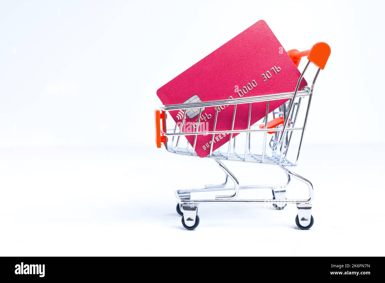 Large pink bank card in a miniature push trolley isolated on white ...