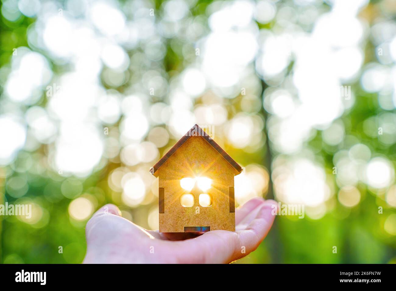Freshly built small wooden house in hand against a defocused natural ...