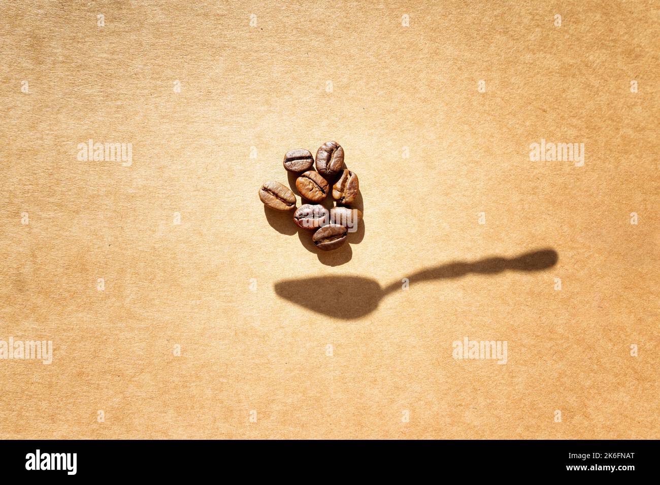 Pile of roasted coffee beans and a spoon shadow silhouette on a craft ...