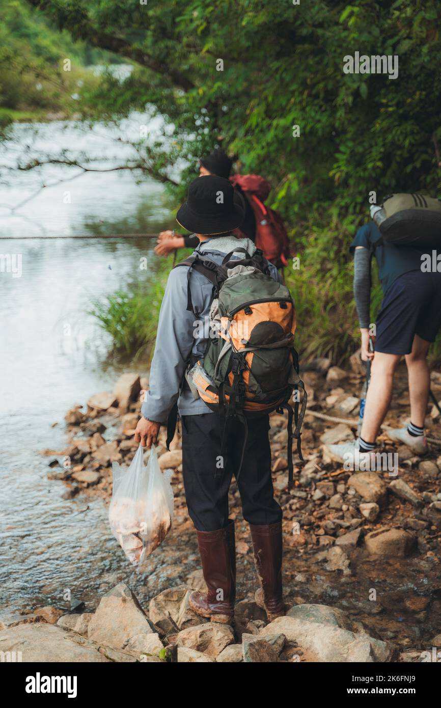 A vertical shot of people fishing on the riverside near the forest ...