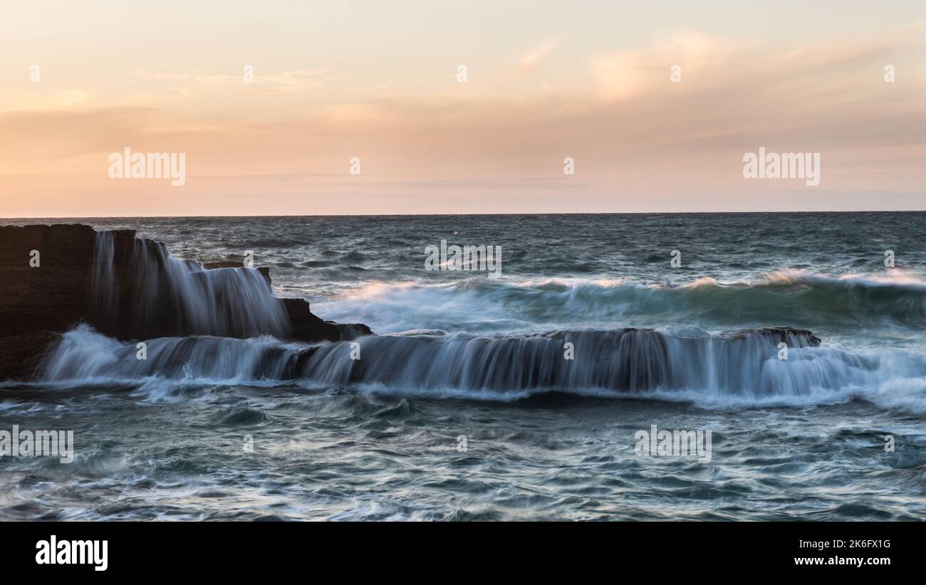 Waves cascading over rocks in the sea causing little waterfalls Stock ...
