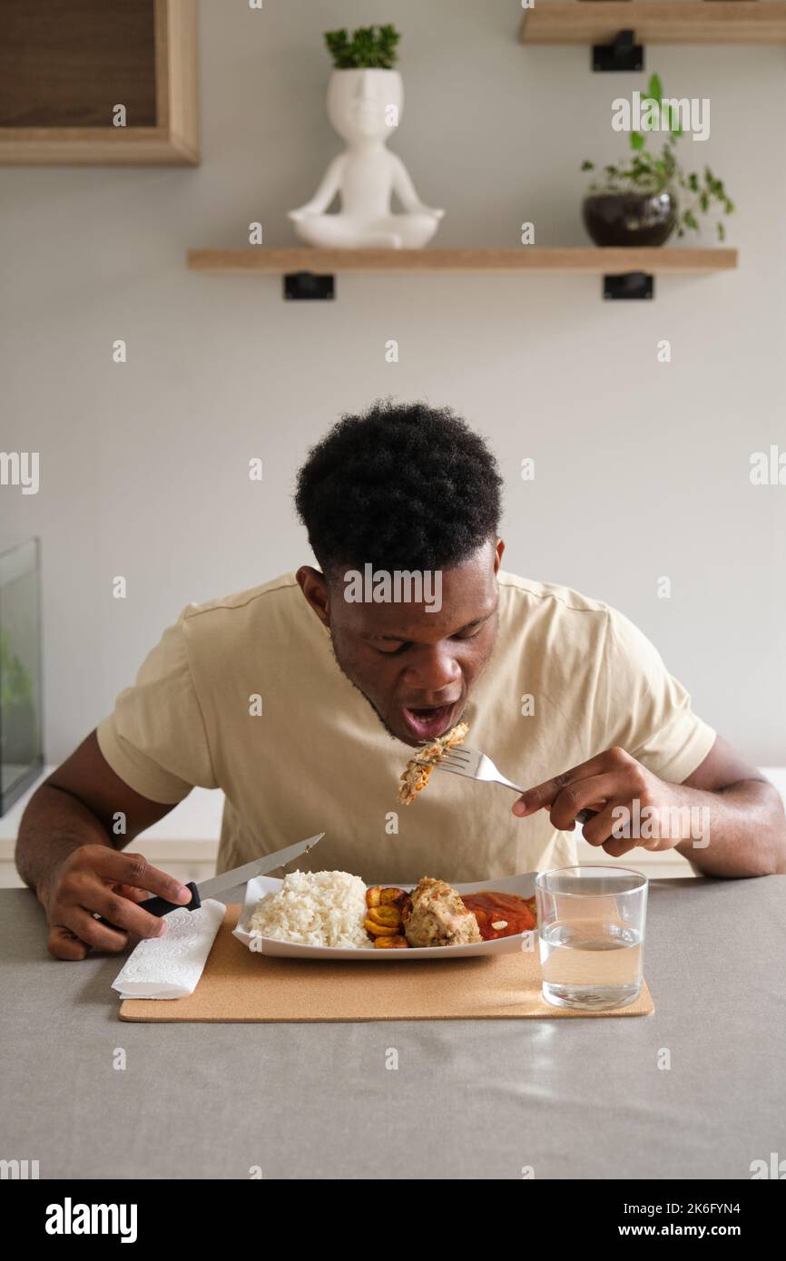 Young black man eating fried chicken, rice and plantain with tomato ...