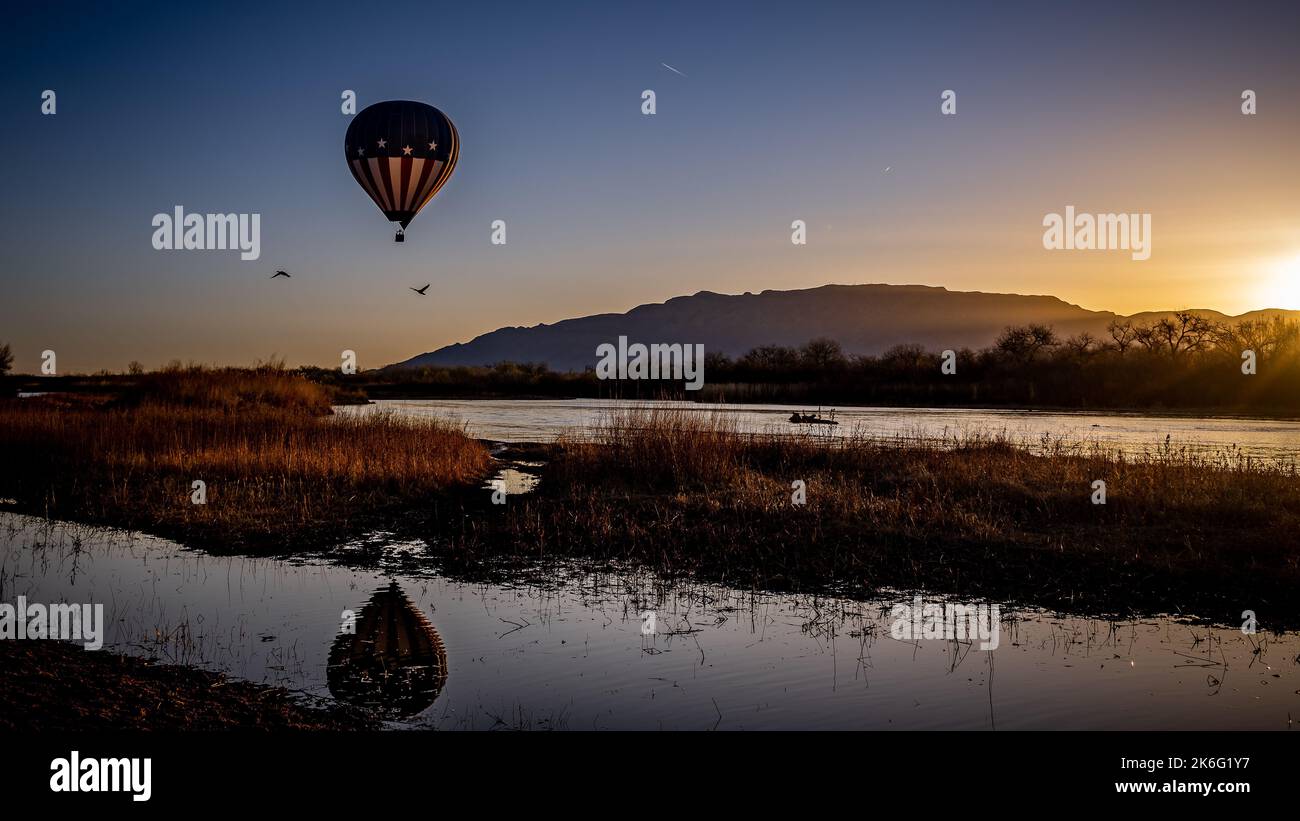 A hot air balloons over the Rio Grande river at sunrise next to flying ...