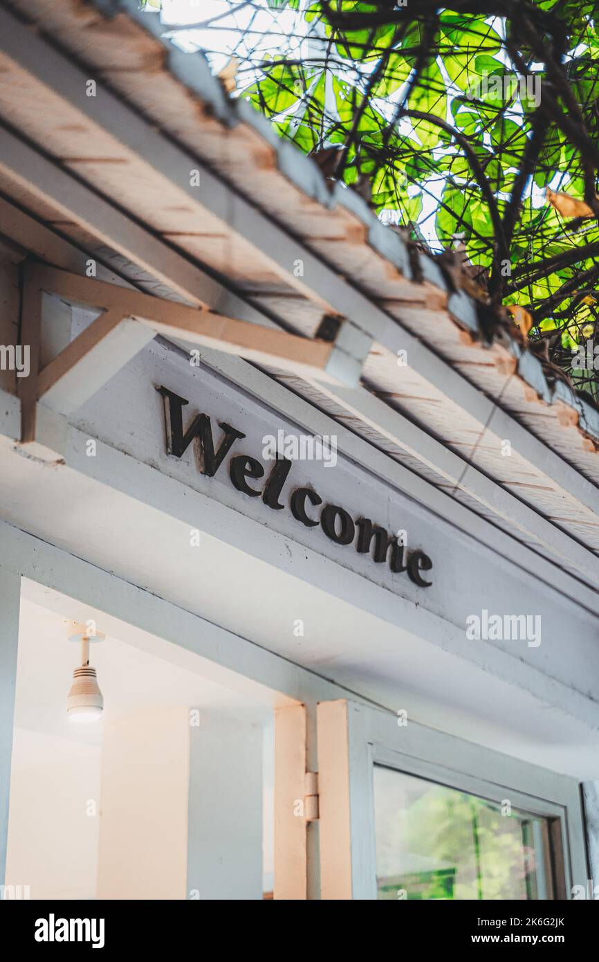 A vertical of the "Welcome" text with black letters on the wall, trees ...
