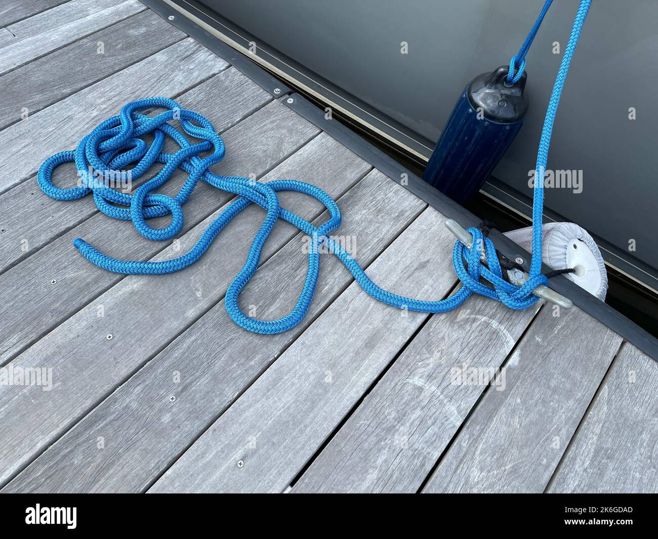 A closeup of a blue rope moor knot on the wooden boating deck with ...