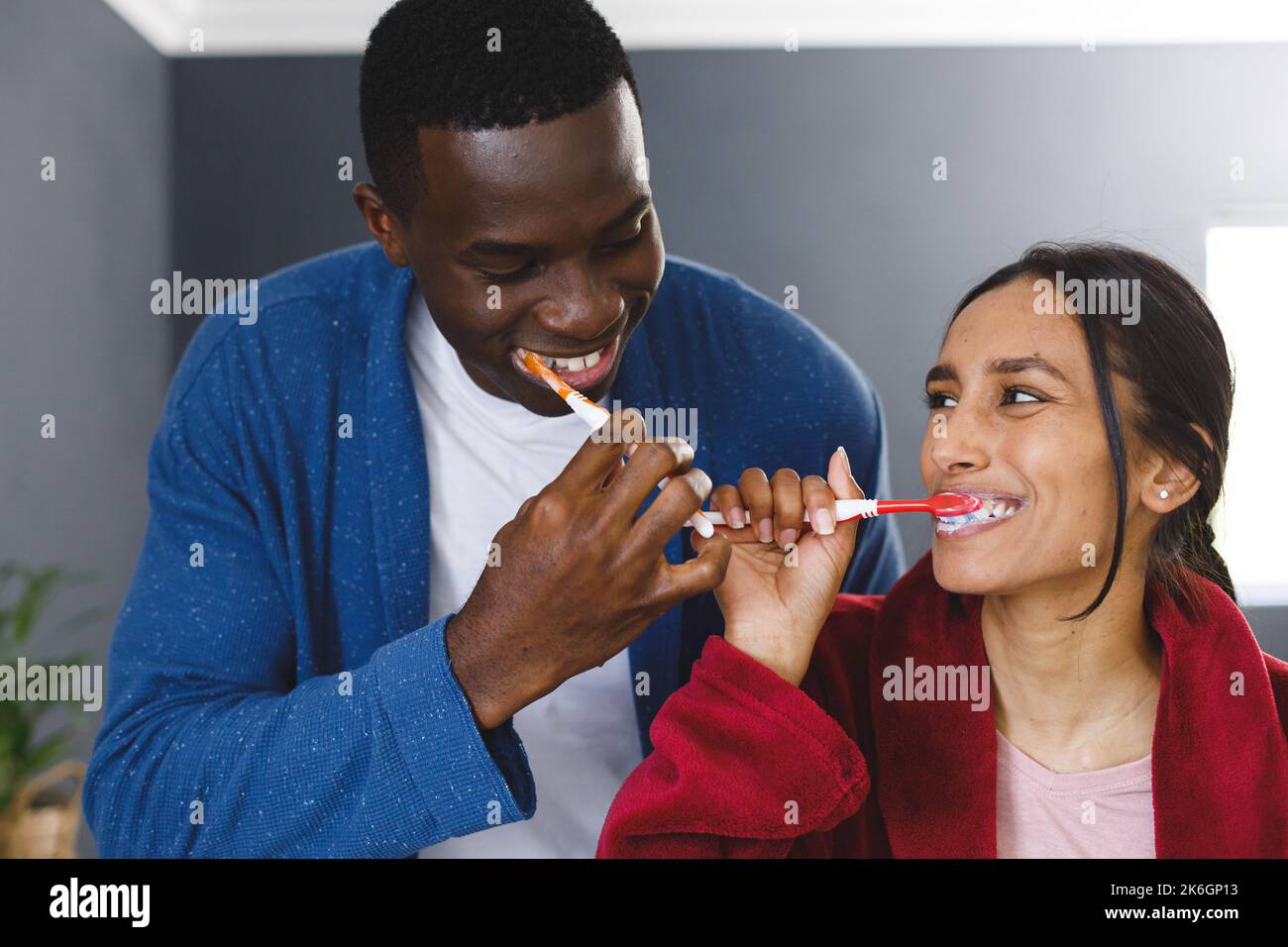Happy diverse couple in brushing teeth in bathroom, looking at each ...