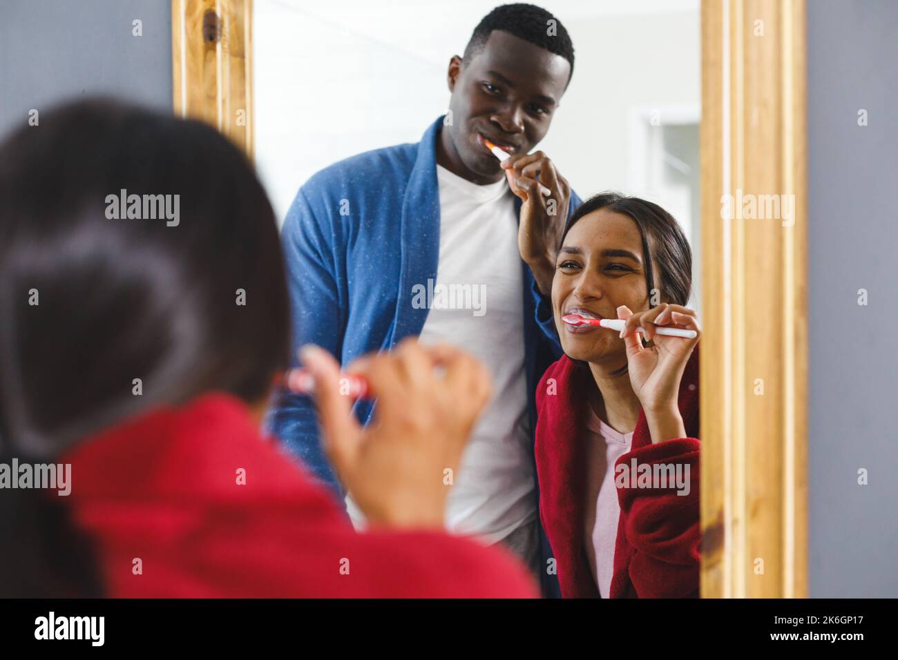 Happy diverse couple in brushing teeth in bathroom, looking in mirror ...