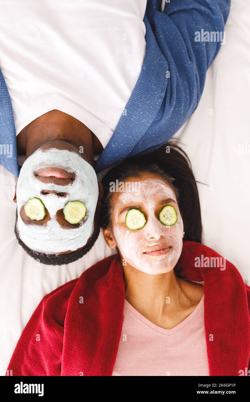 Vertical image of diverse couple in cleansing face masks with cucumber ...