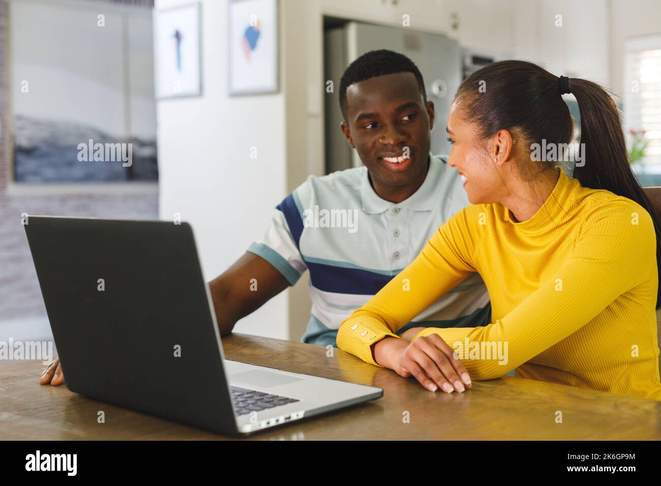Happy diverse couple using laptop smiling at each other in kitchen ...