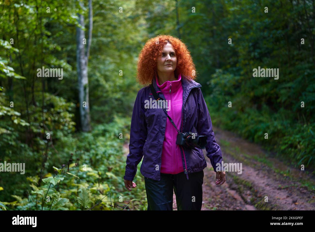 Redhead woman with curly hair and camera hiking on a trail in the ...