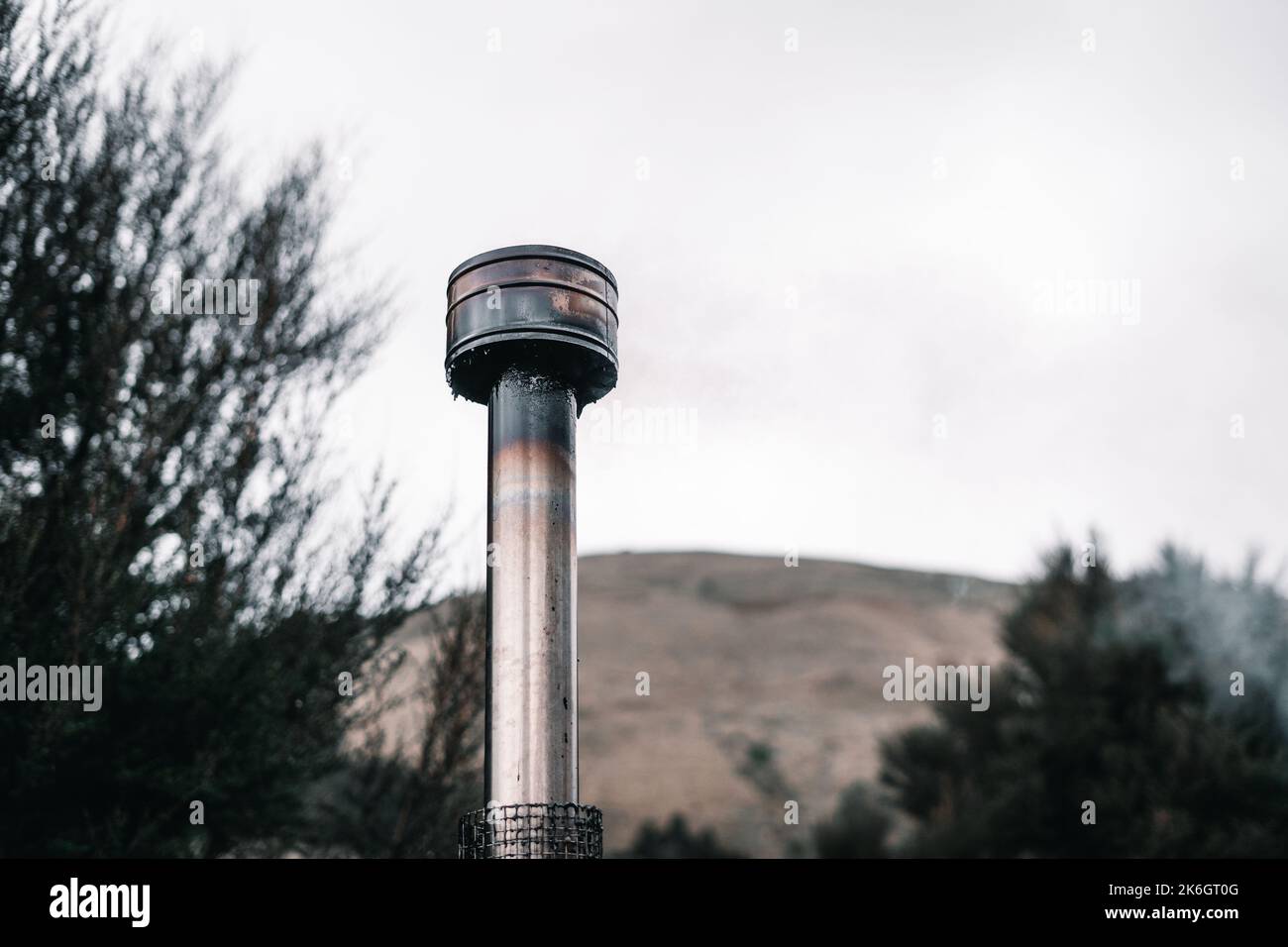 metallic warm smoking chimney in the middle of nature and trees near ...
