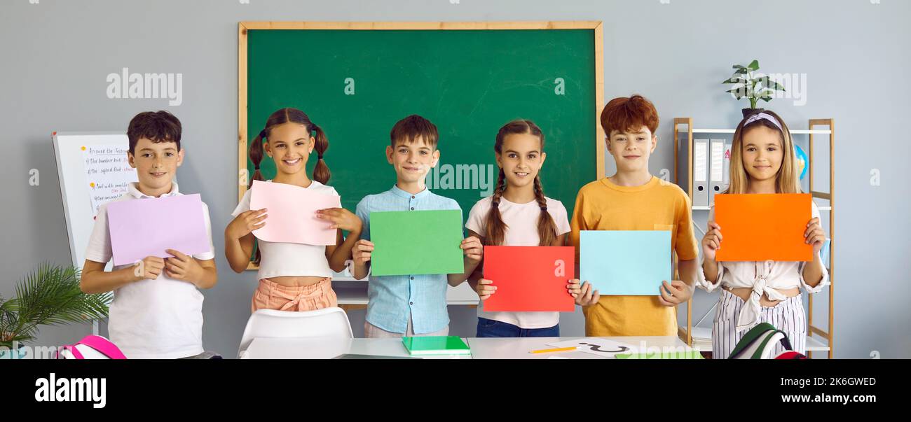 Group of happy school children standing in classroom and holding paper ...