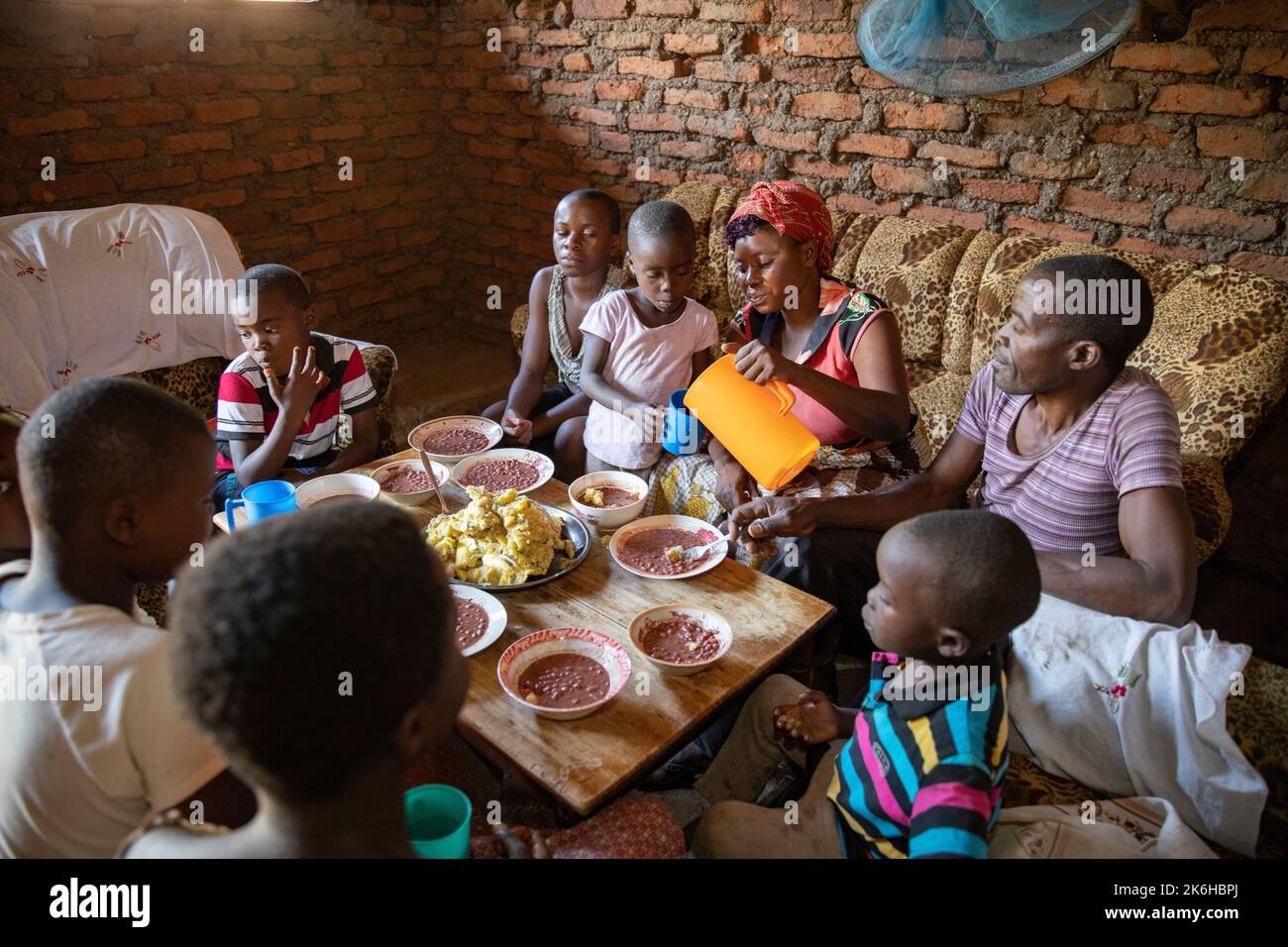 Ugandan family sharing a meal of beans and mashed savory bananas ...