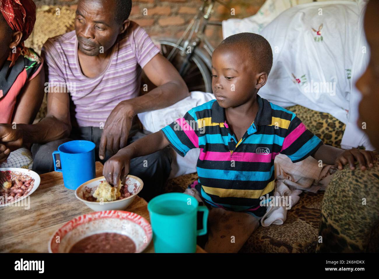 Ugandan family sharing a meal of beans and mashed savory bananas ...