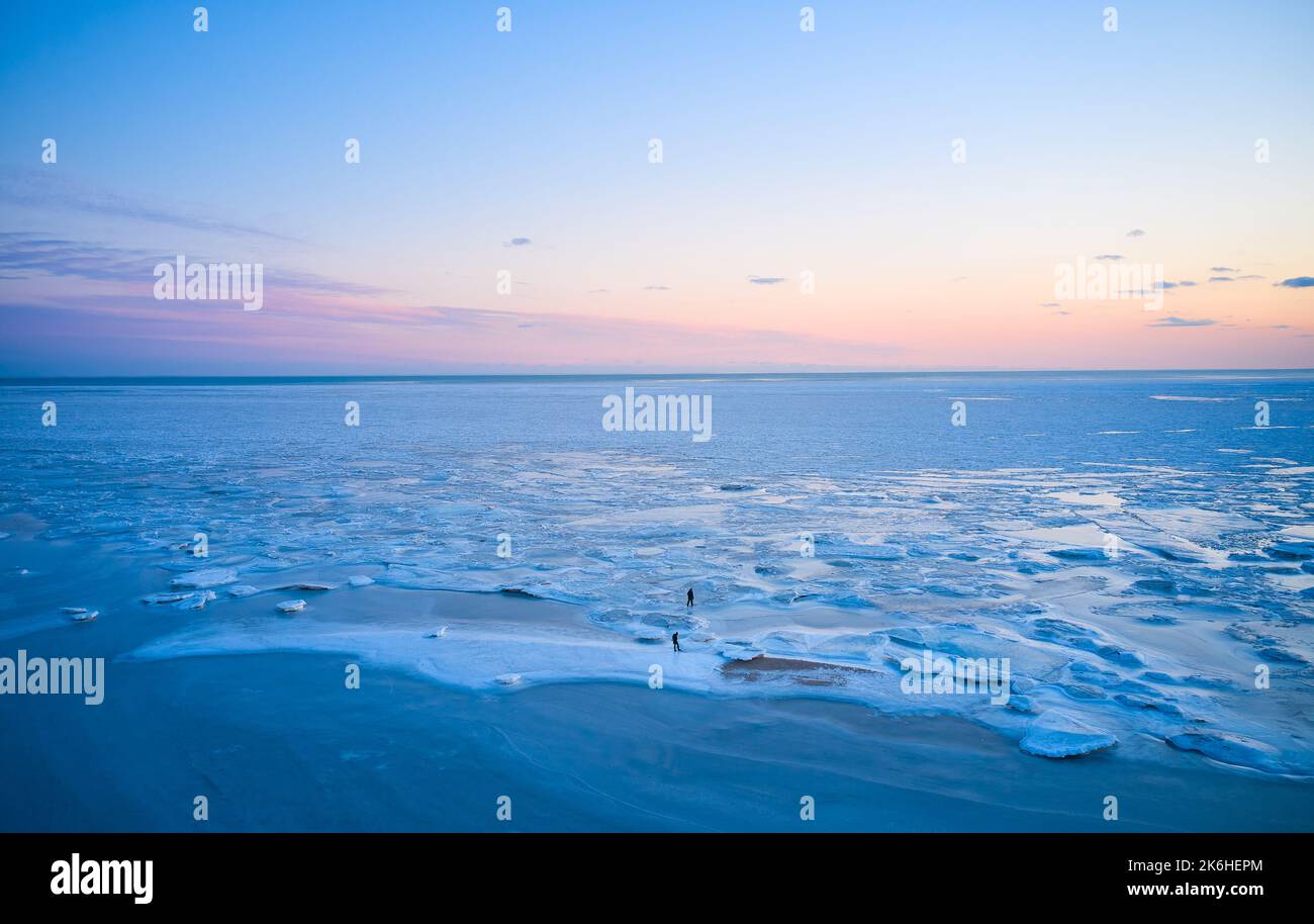 Aerial view - two people walk on ice on sunset over the frozen sea ...