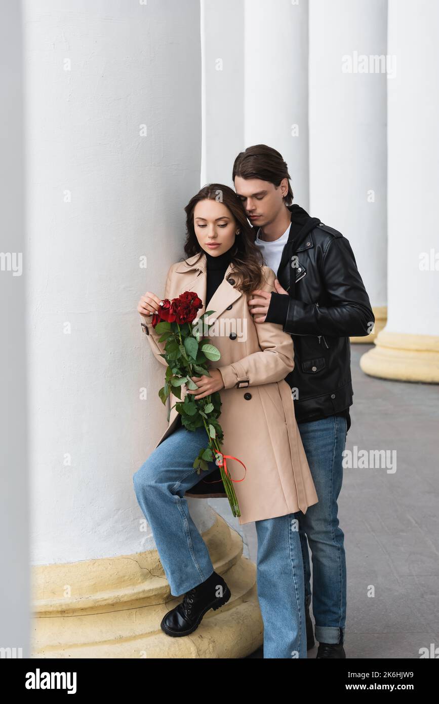 full length of stylish young man hugging pretty woman in beige trench ...