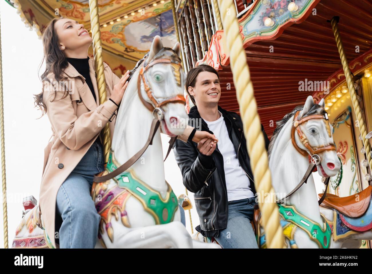 happy young couple holding hands and riding carousel horses in ...