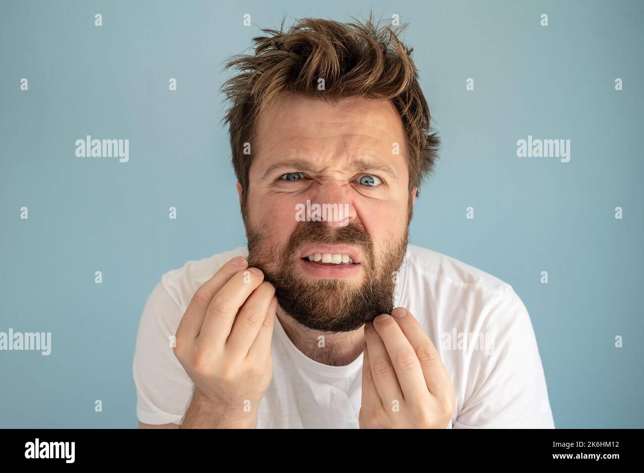 Man with a tousled hairstyle and an untidy beard, touches his stubble ...