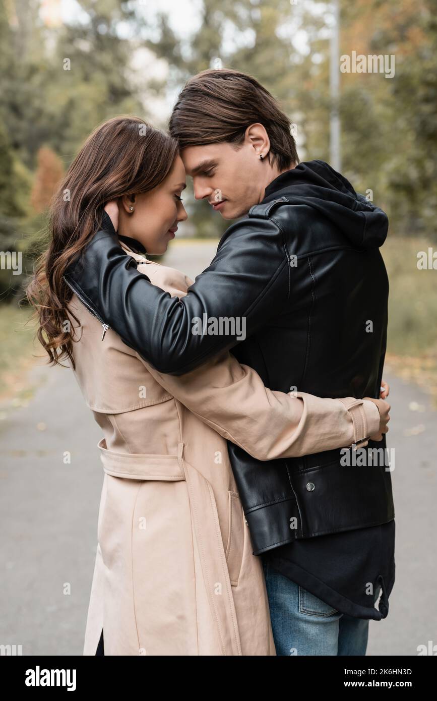 side view of stylish young man hugging pretty girlfriend in trench coat ...