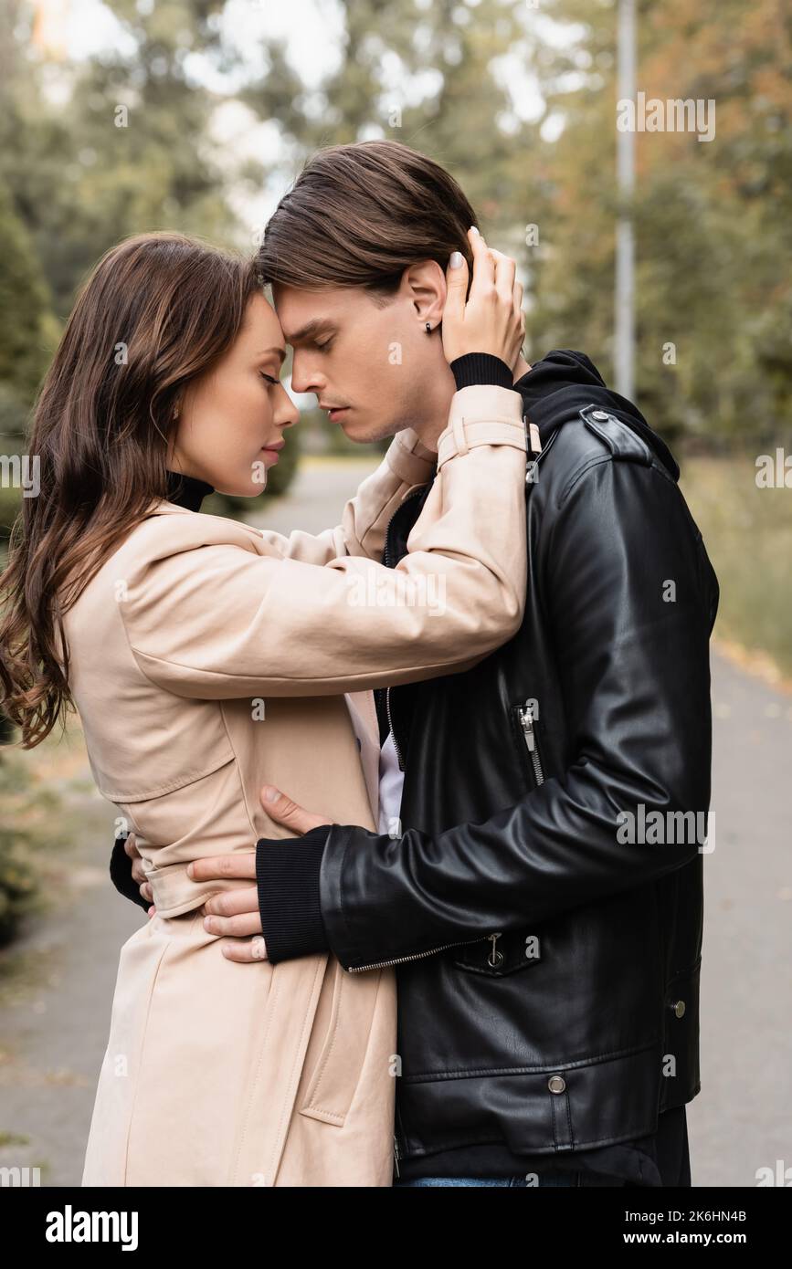side view of young woman in beige trench coat hugging boyfriend in ...