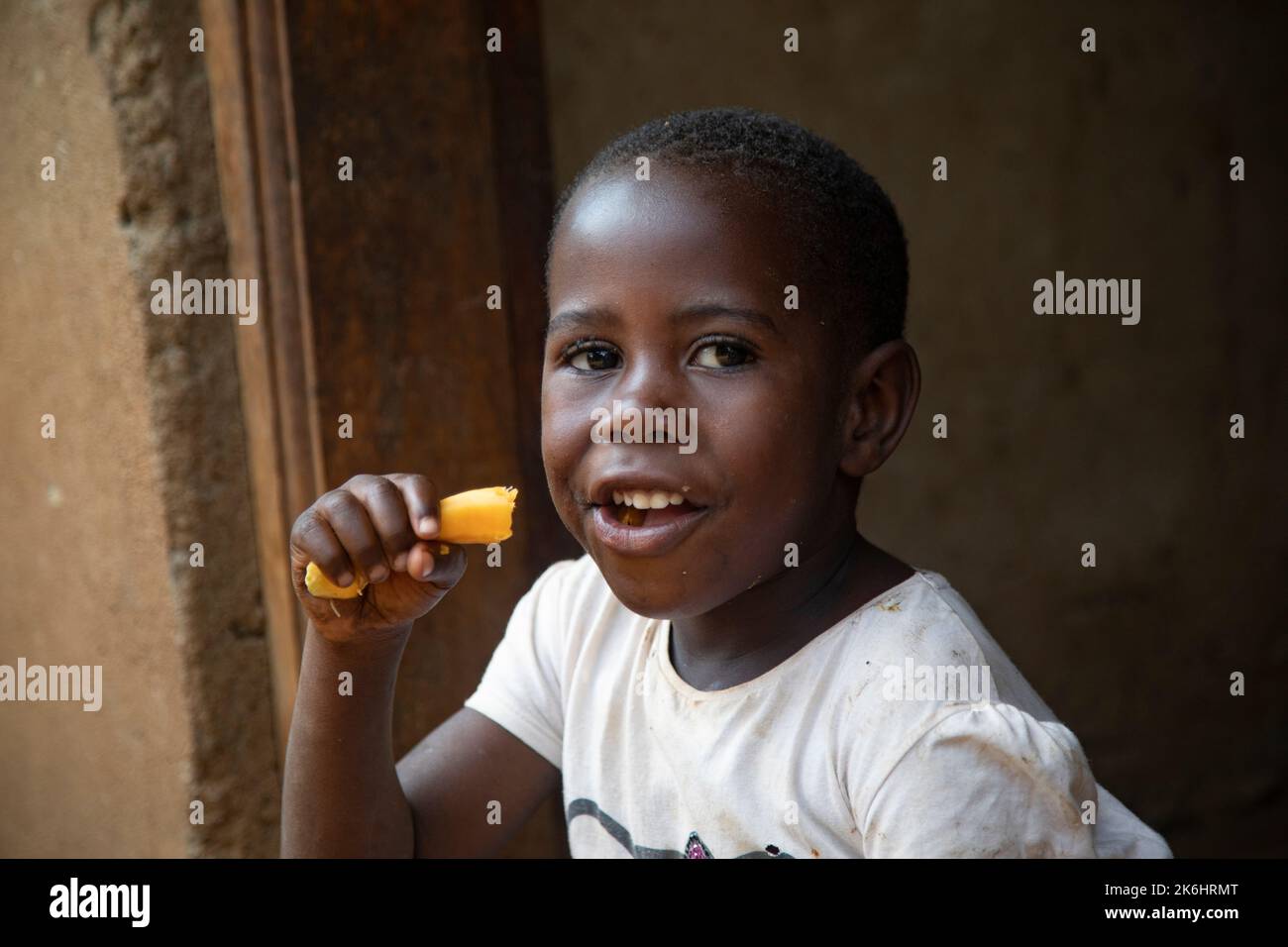 A cute young boy eats a bite of mango fruit at his home in Kasese ...
