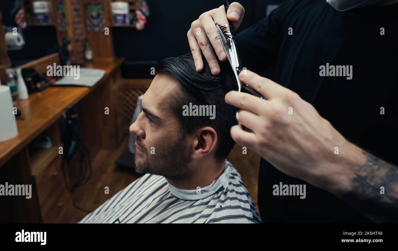 Barber cutting hair of customer in hairdressing cape in barbershop ...