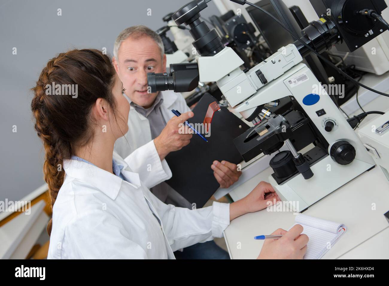 Teacher talking to student sat at microscope Stock Photo - Alamy