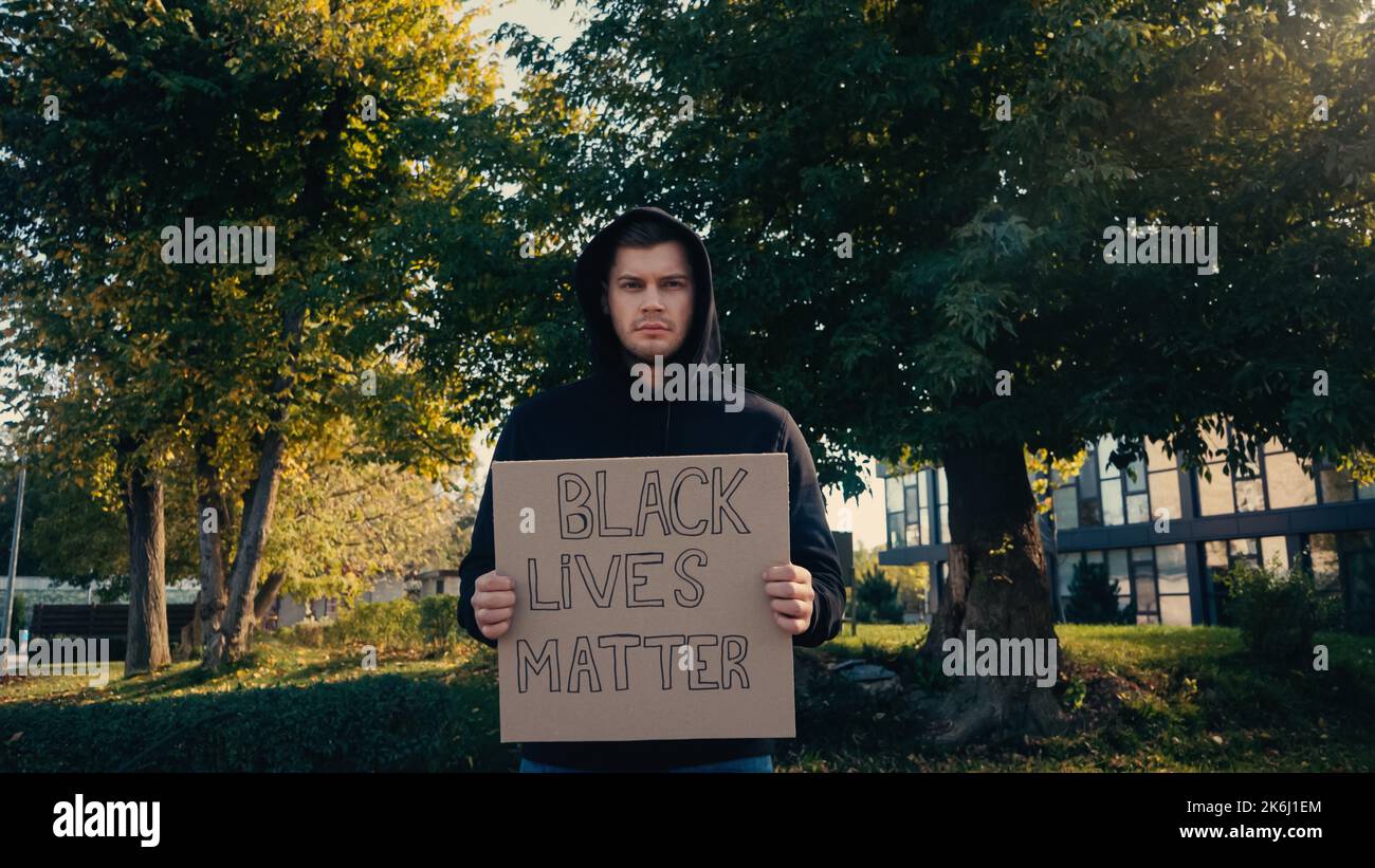 young man in hoodie holding placard with black lives matter lettering ...
