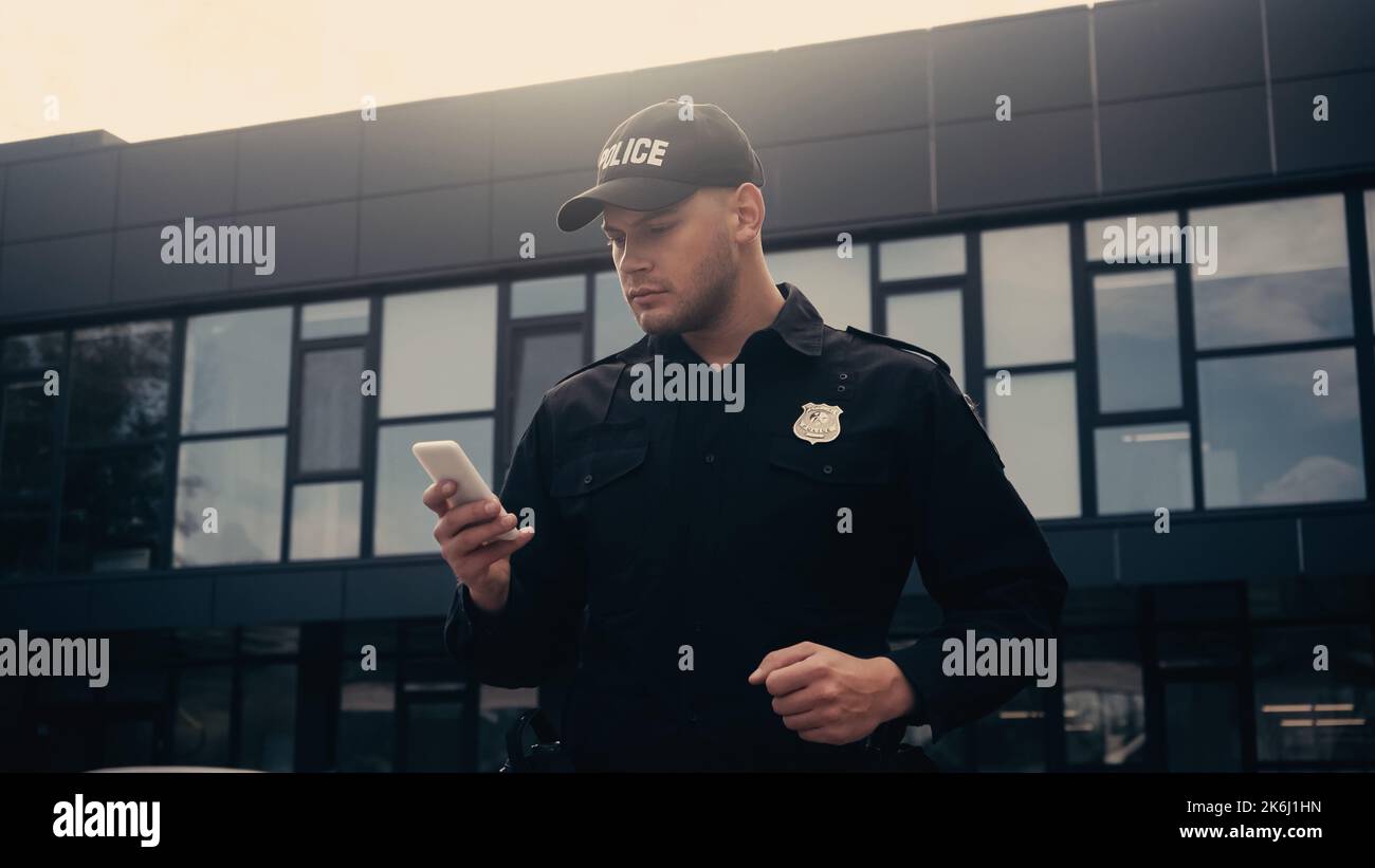 policeman in uniform and badge using smartphone on urban street,stock ...