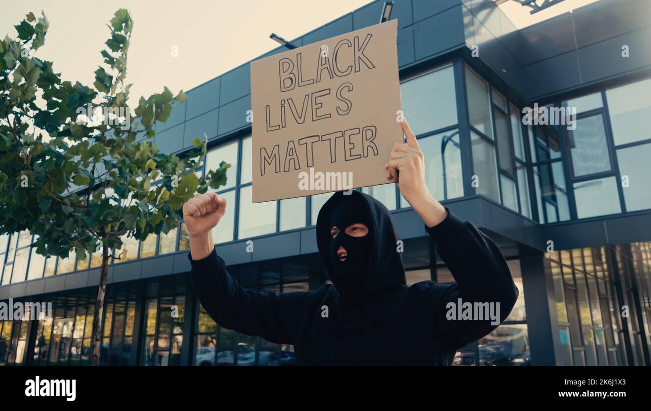 young activist in balaclava holding placard with black lives matter ...